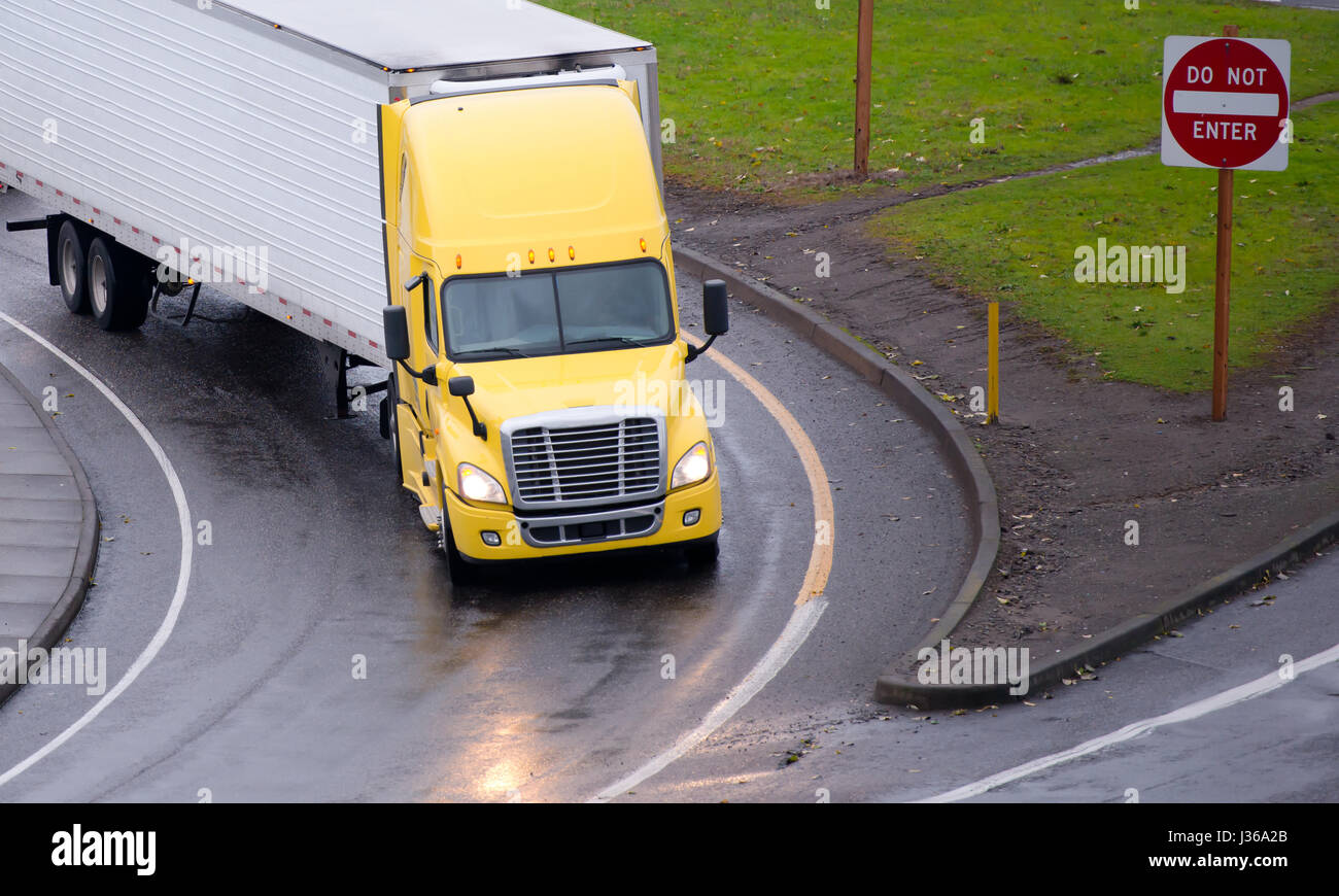 Modern yellow big rig semi-truck with lights on with dry van trailer at ...