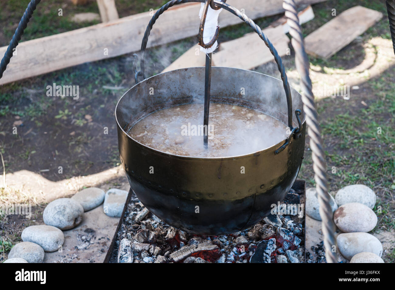 Black cauldron hangs on a hook over the open fire in a medieval camp ...