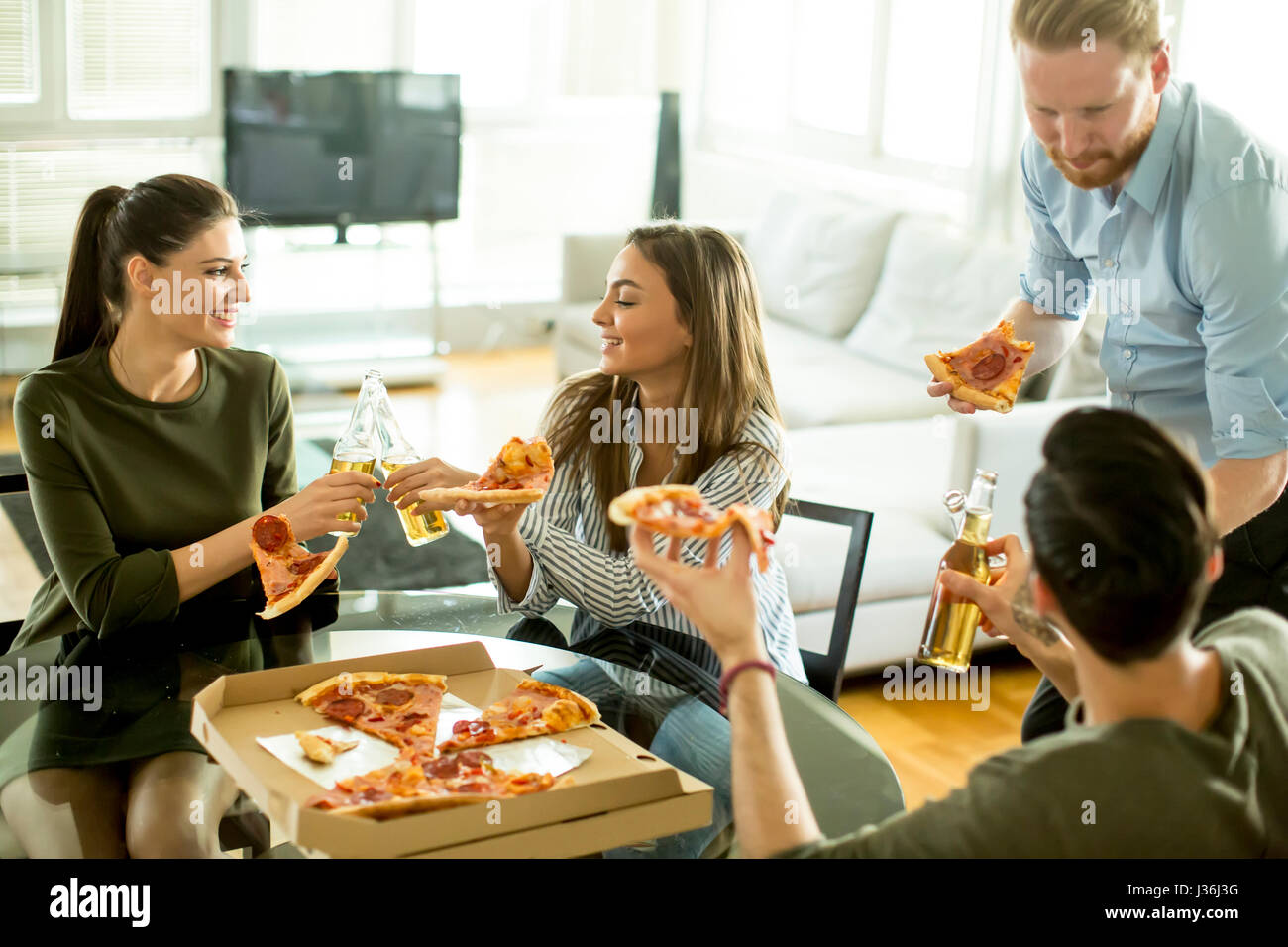 Group of cheerful young people eating pizza in the room and having fun ...
