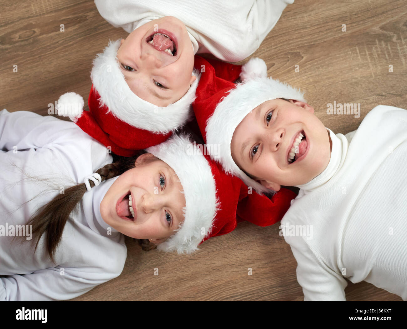 three kids in Santa hats lying on wooden background, having fun and ...