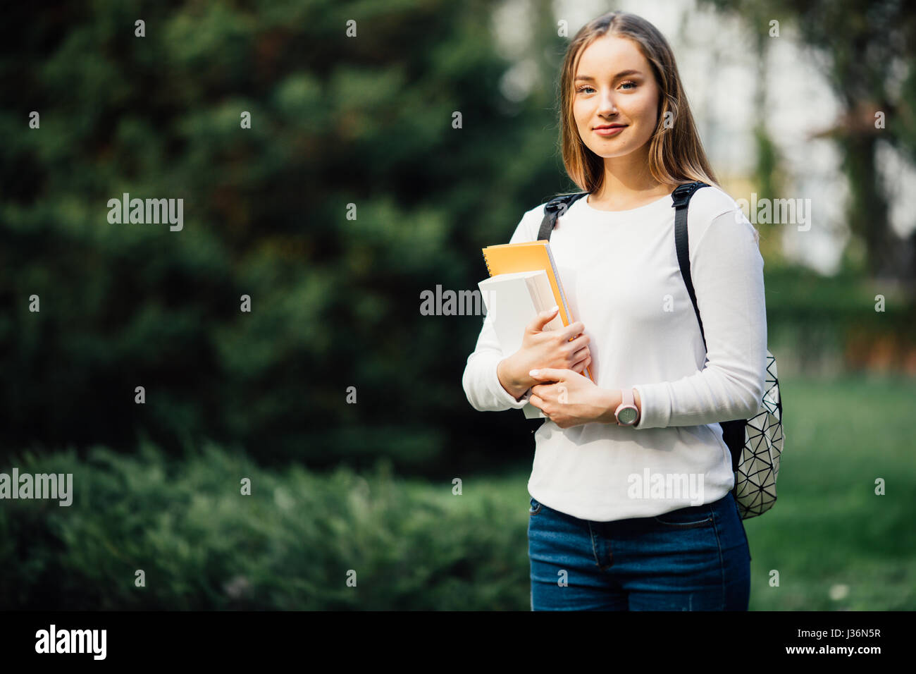 Student girl portrait holding books wearing backpack outdoor in park ...