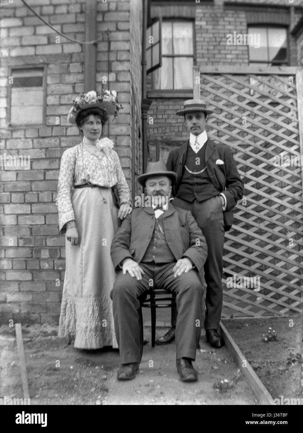 Edwardian family of three pose for a portrait in the backyard of a ...
