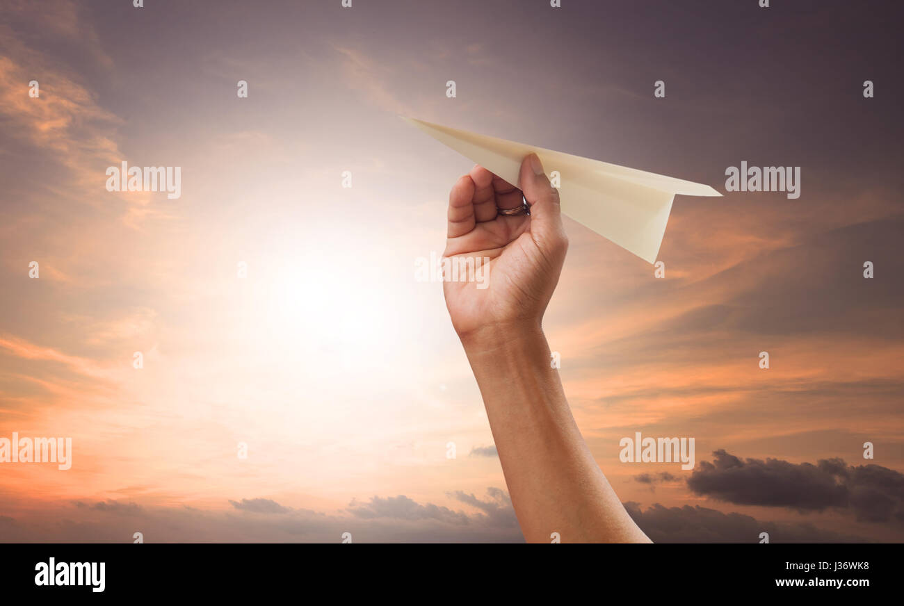 hand preparing to throwing paper plane to mid air againt green grass ...