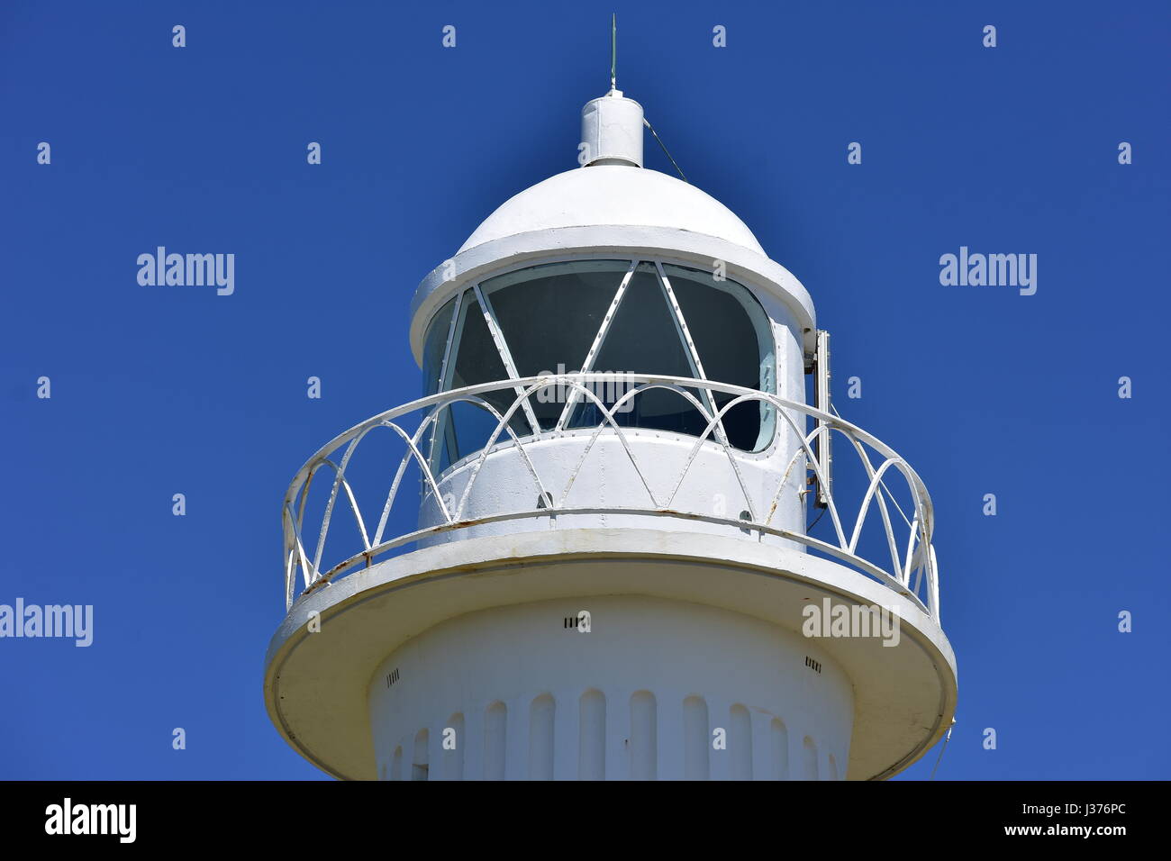 Top part of white lighthouse showing circular railing and glass panes ...