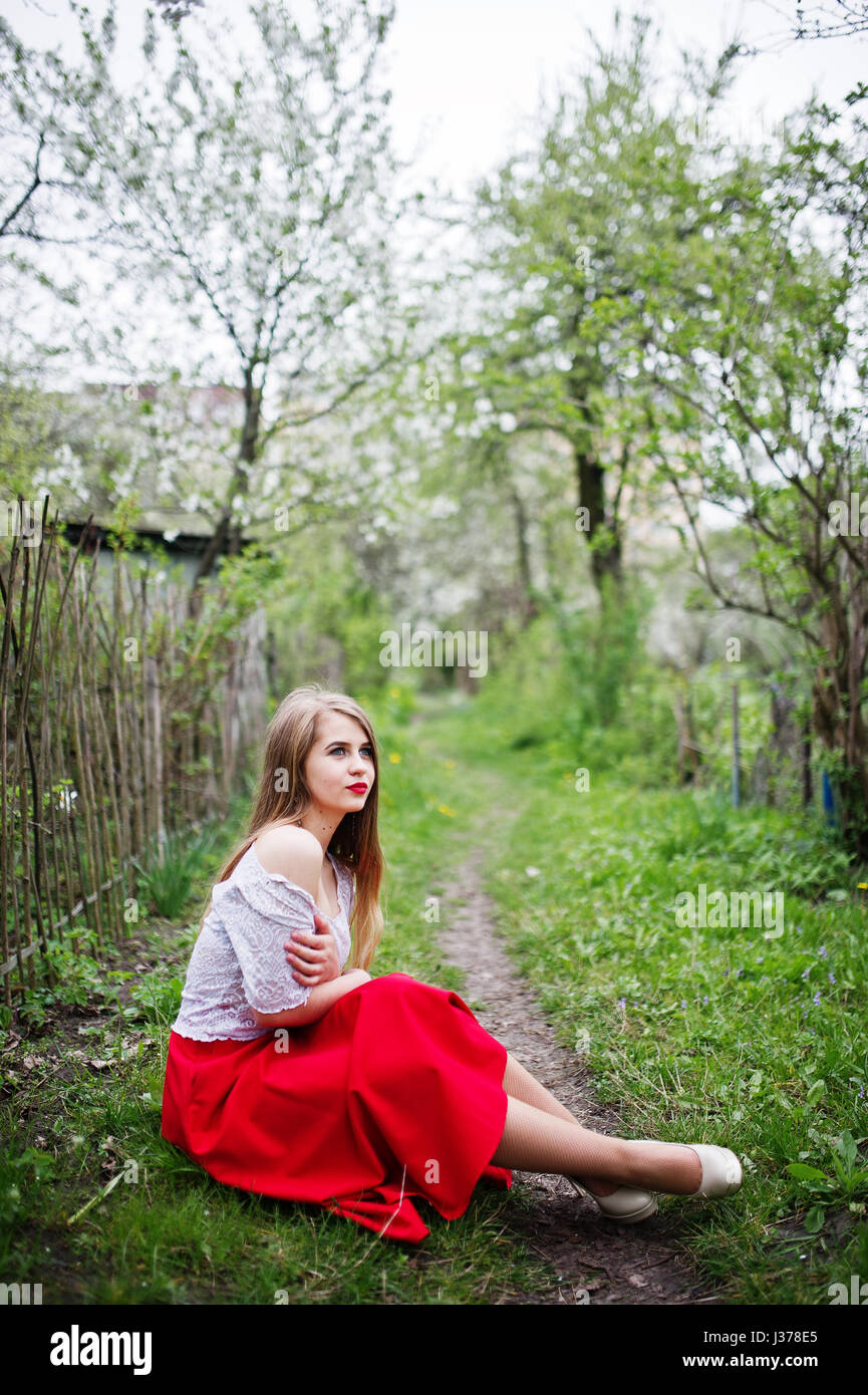 Portrait of sitting beautiful girl with red lips at spring blossom garden on green grass, wear ...