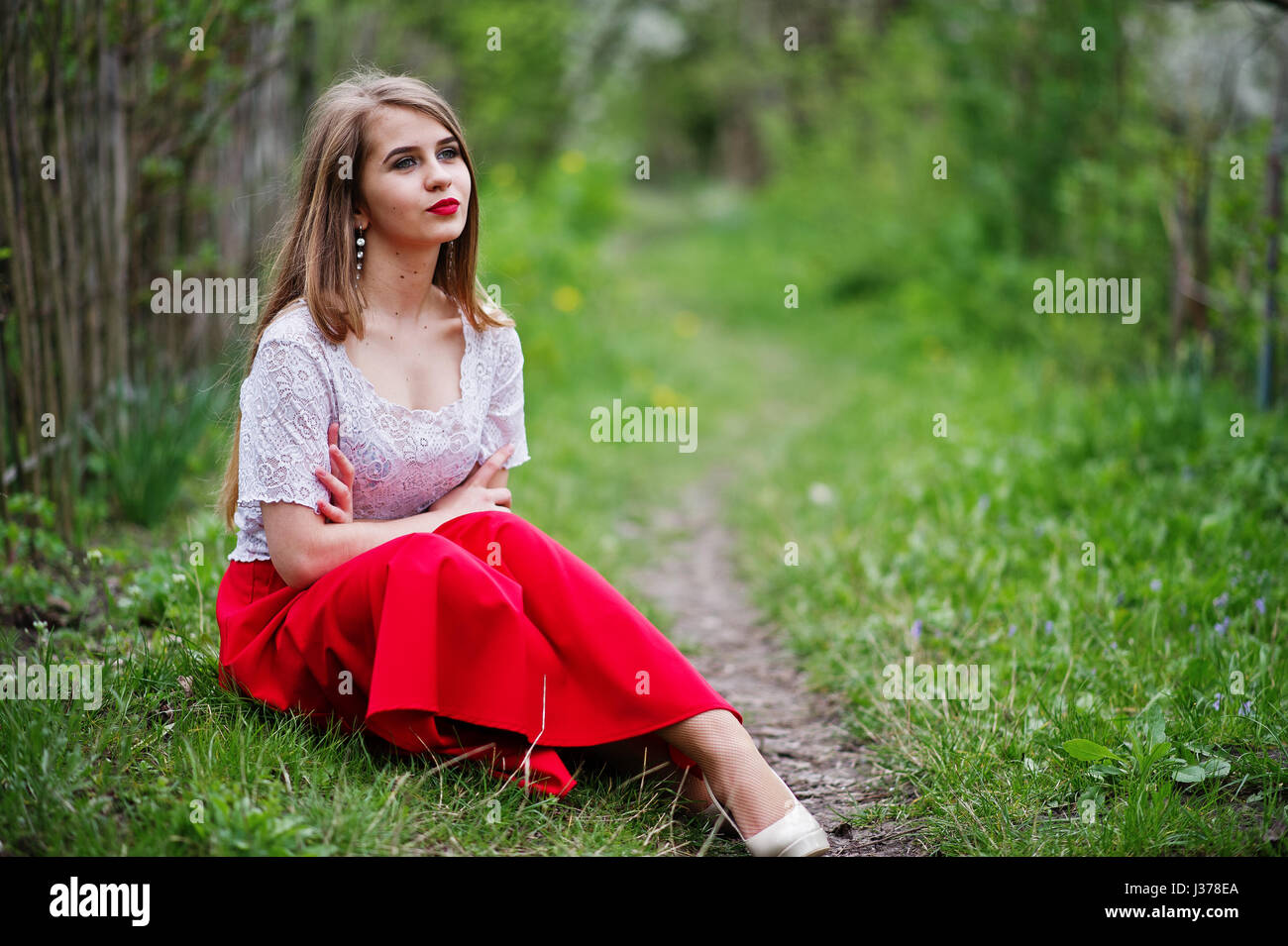 Portrait of sitting beautiful girl with red lips at spring blossom garden on green grass, wear ...