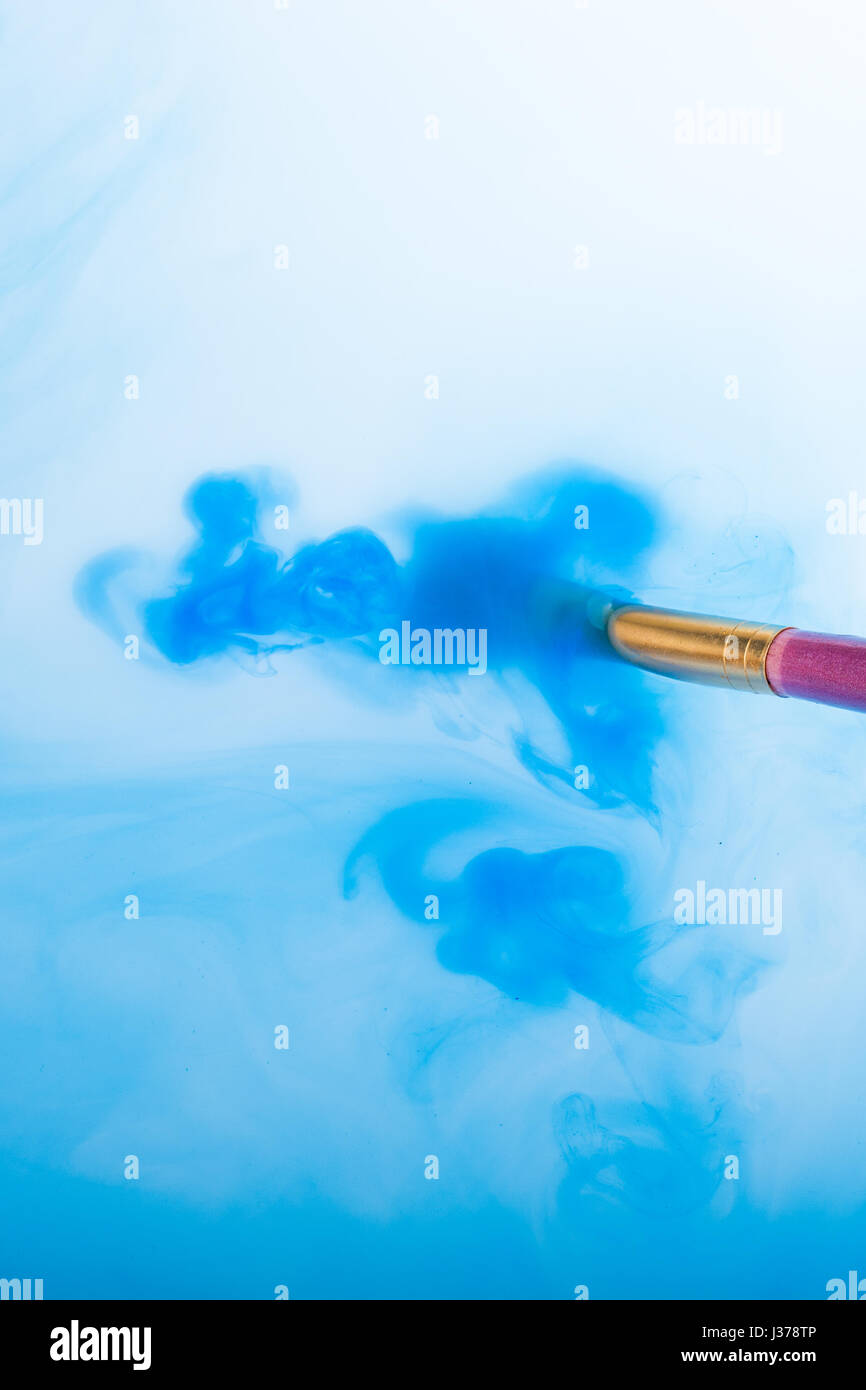 Watercolor paint dissolving in water as painting brush touches water ...