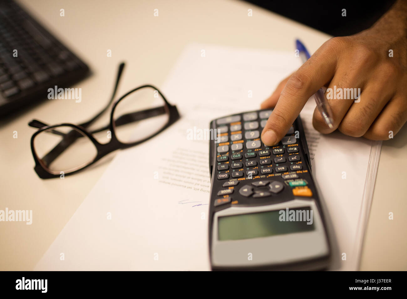 Cropped hand on business person using calculator by eyeglasses on desk ...