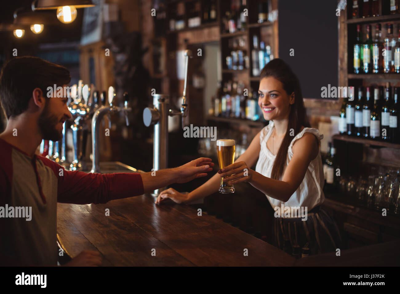 Female bar tender giving glass of beer to customer at bar counter Stock ...