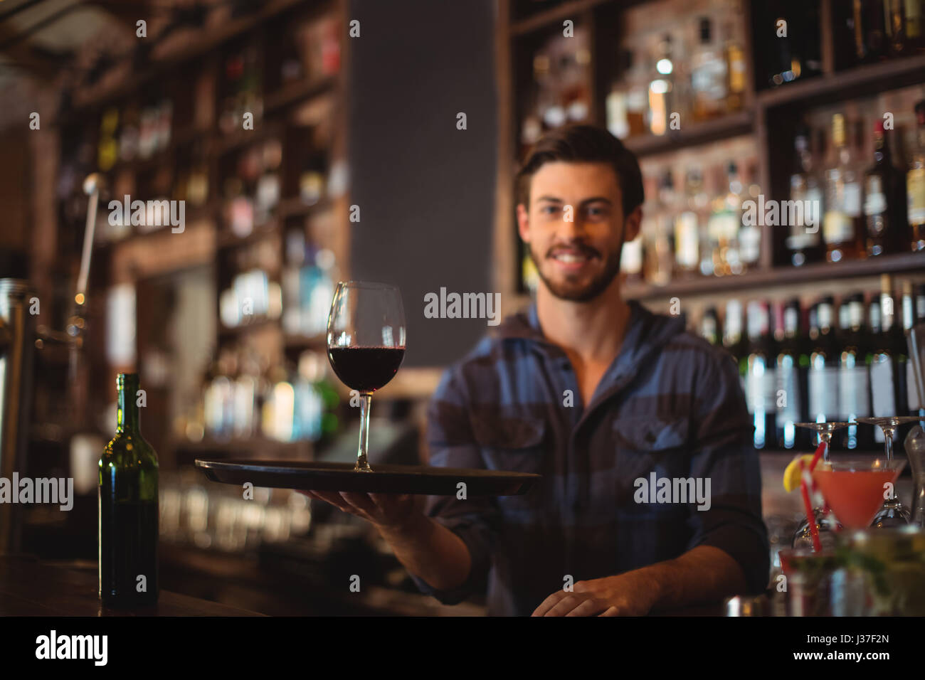 Portrait of bar tender holding a tray with glass of red wine at bar ...
