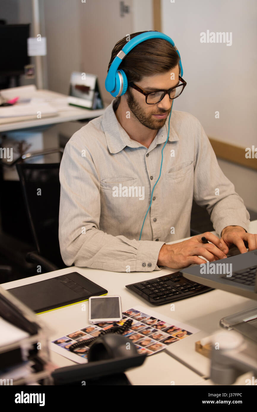 Young businessman listening music through headphones while working at ...