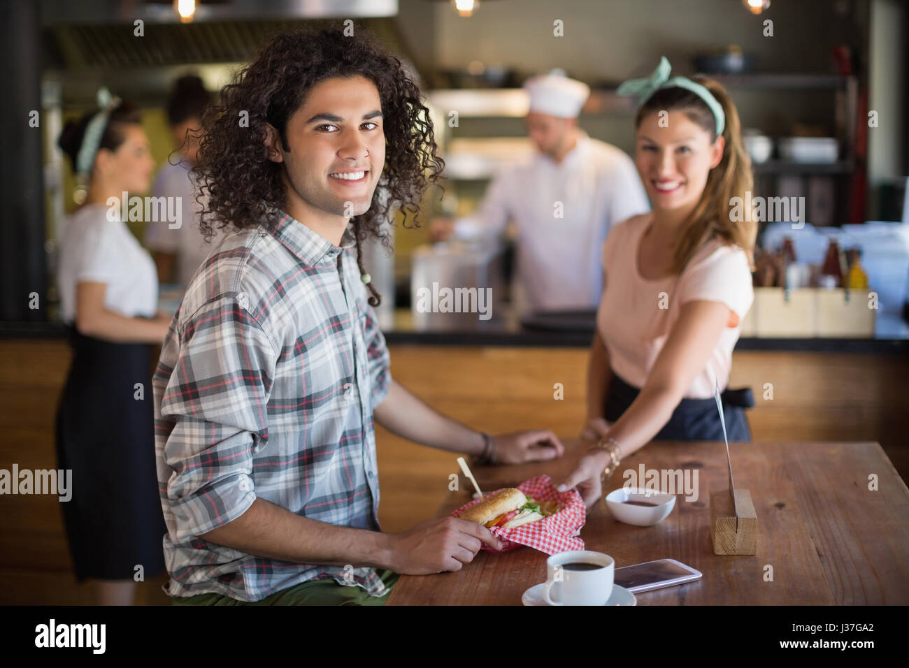 Portrait of waitress serving burger to young man in restaurant Stock ...