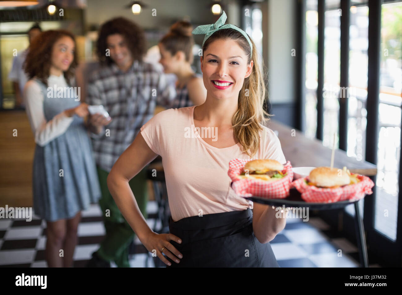 Portrait of smiling young waitress serving burger with customers in ...
