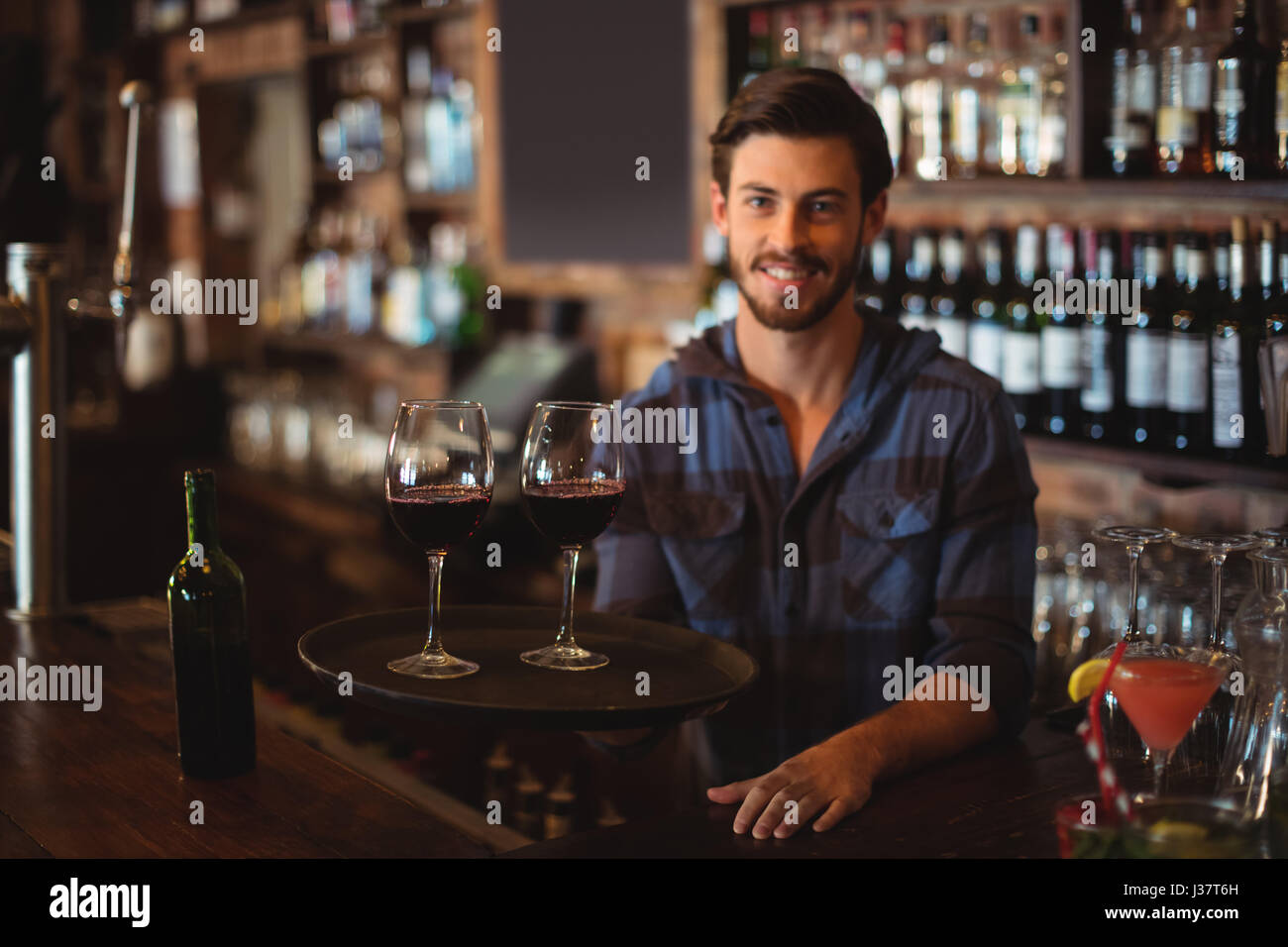 Portrait of bar tender holding a tray with glasses of red wine at bar ...