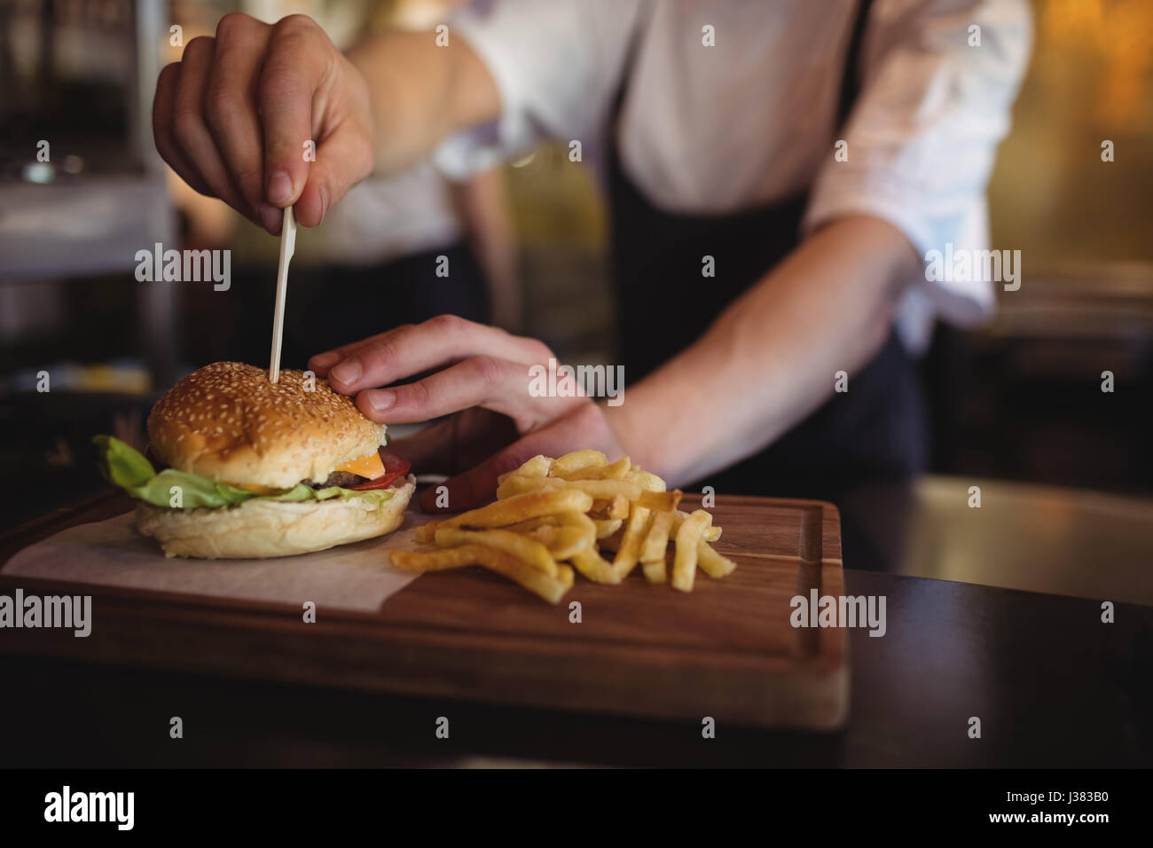 Close-up of chef placing tooth pick over burger at order station in the ...