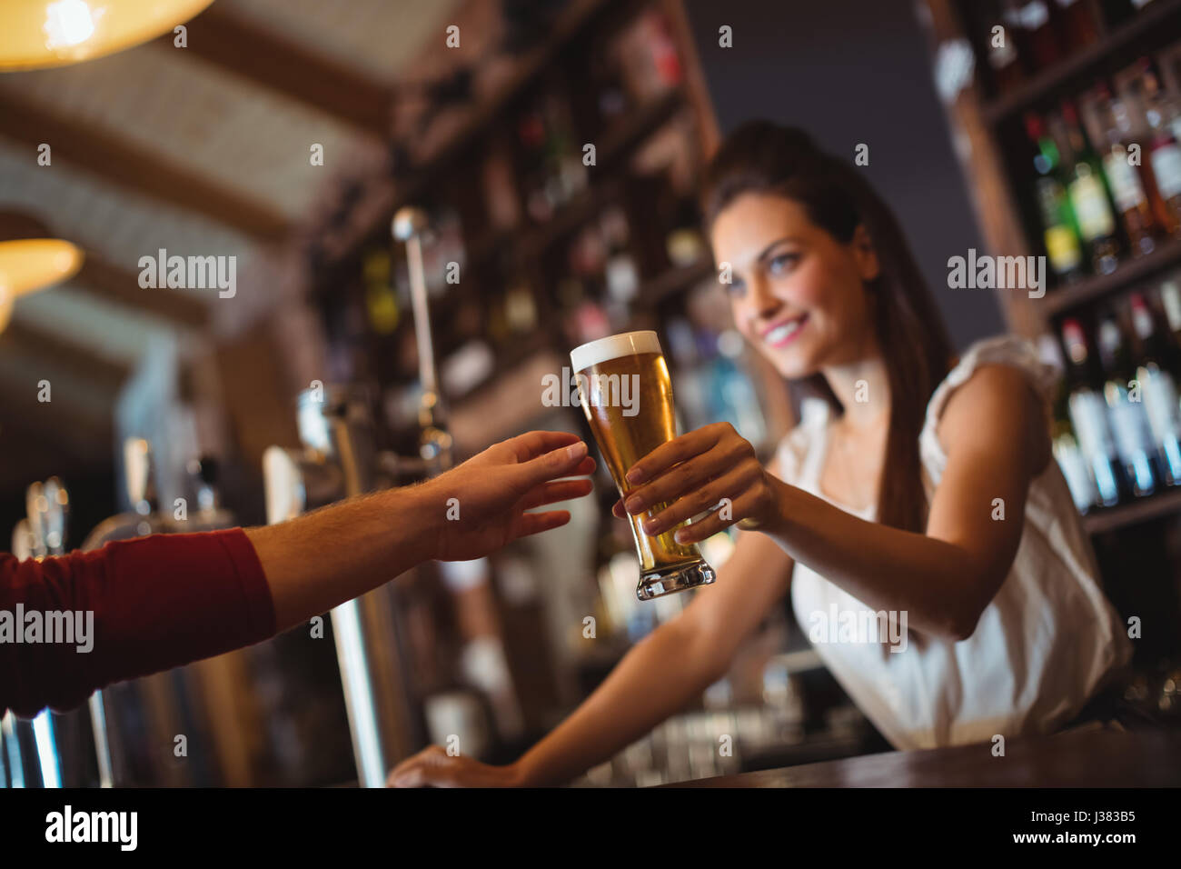 Female bar tender giving glass of beer to customer at bar counter Stock ...