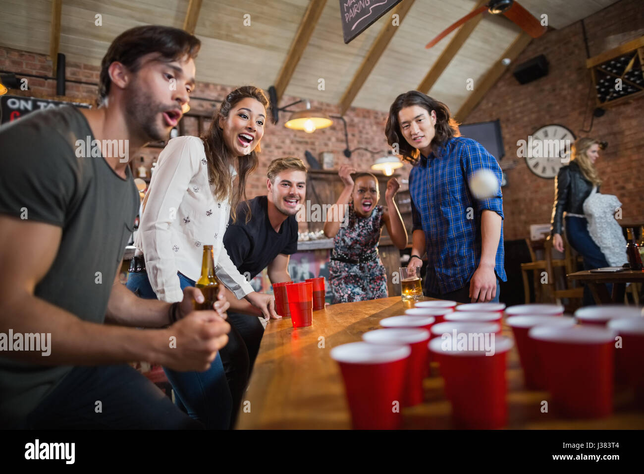 Young friends enjoying beer pong game on table in restaurant Stock ...