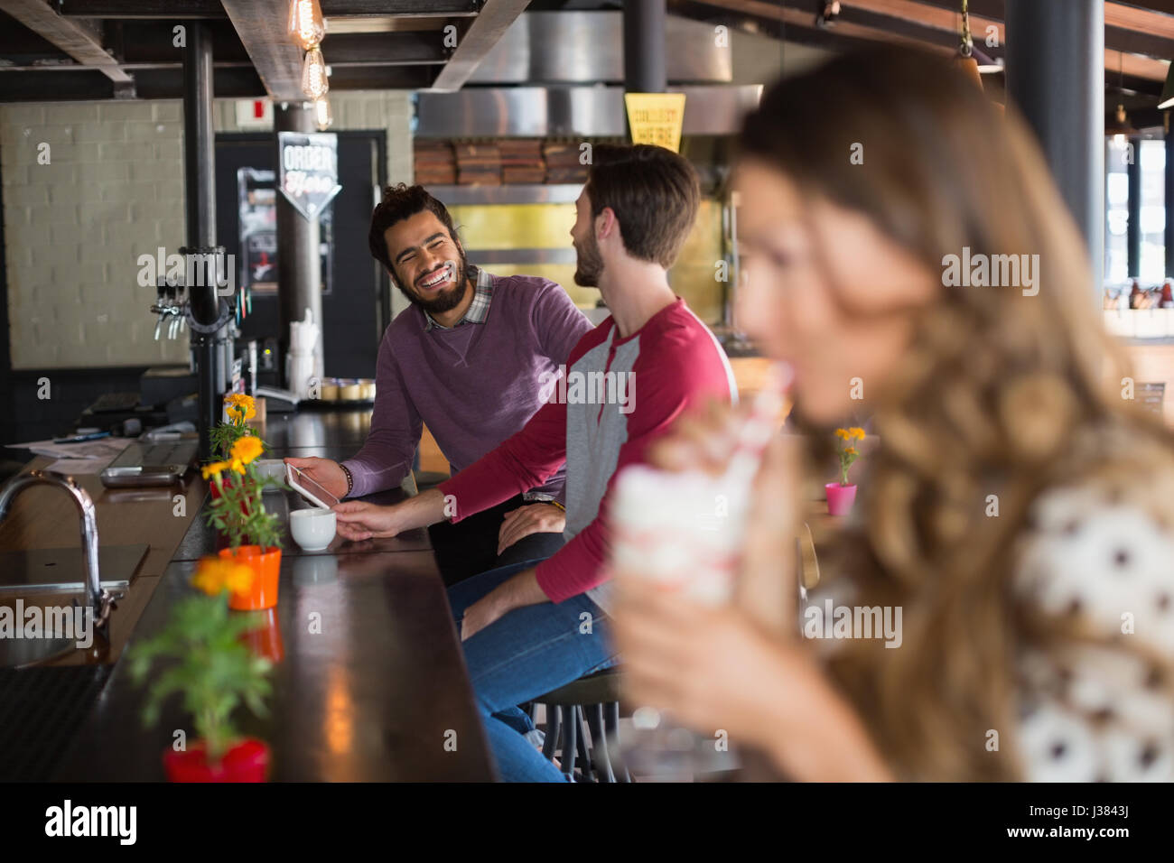 Male friends talking while sitting at counter in restaurant Stock Photo ...
