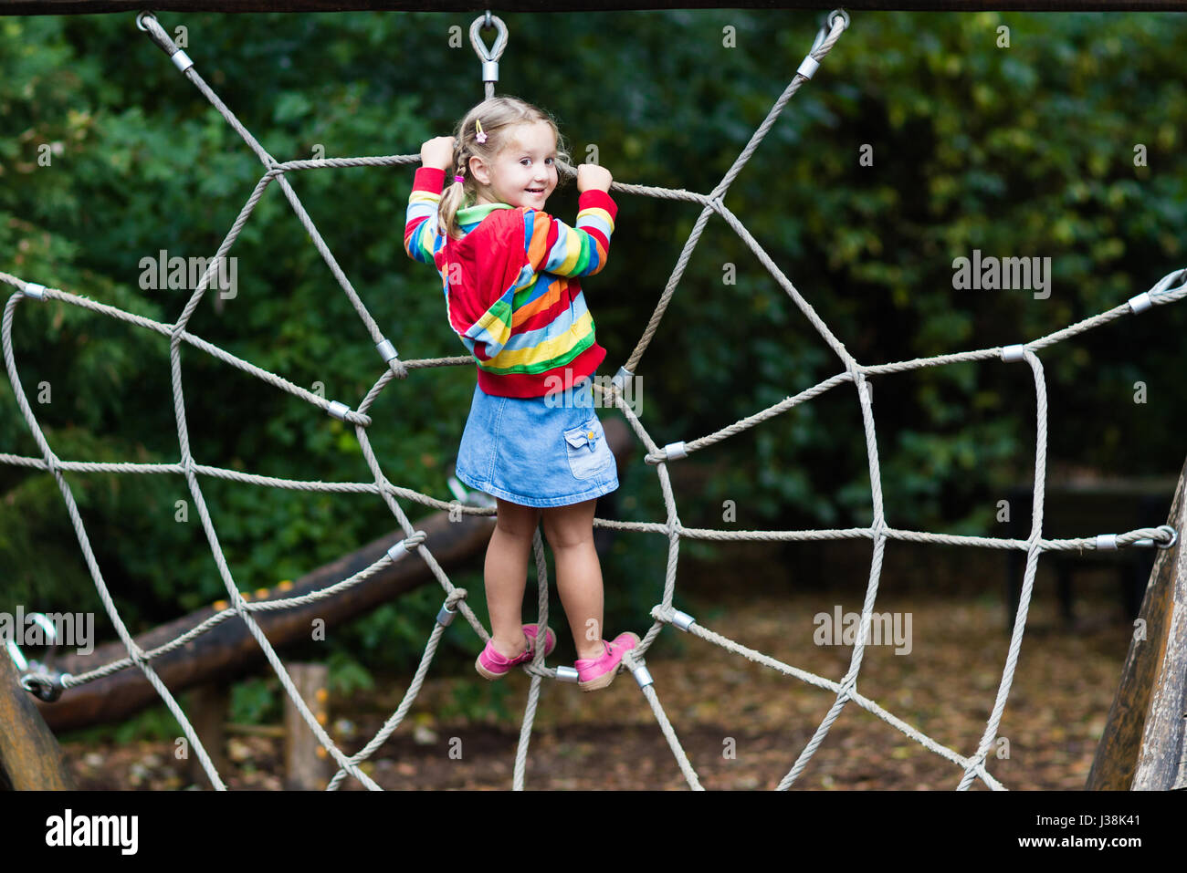 Active little child playing on climbing net and jumping on trampoline ...