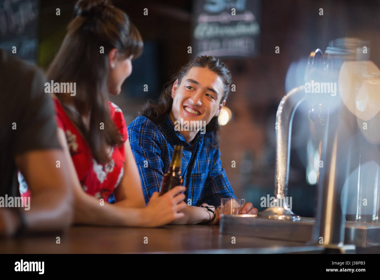 Happy friends looking at each other while leaning on bar counter in pub ...