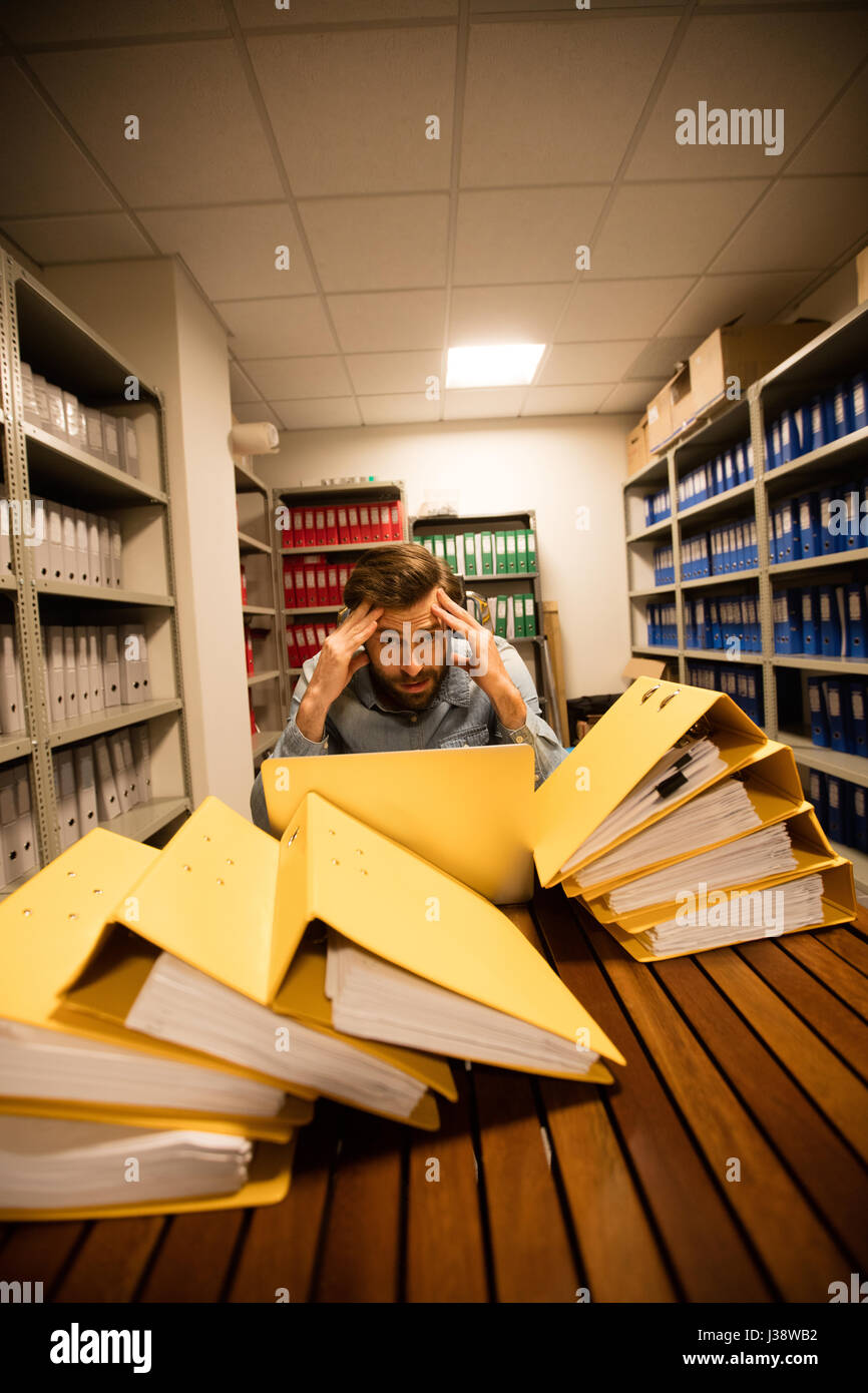 Portrait of frustrated businessman using laptop in file storage room ...