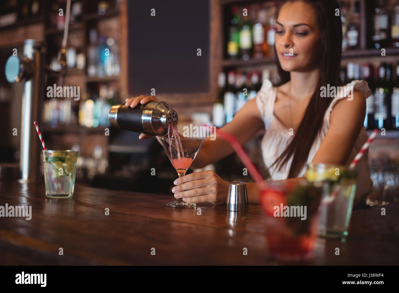 Female bartender pouring cocktail drink in the glass at bar counter ...