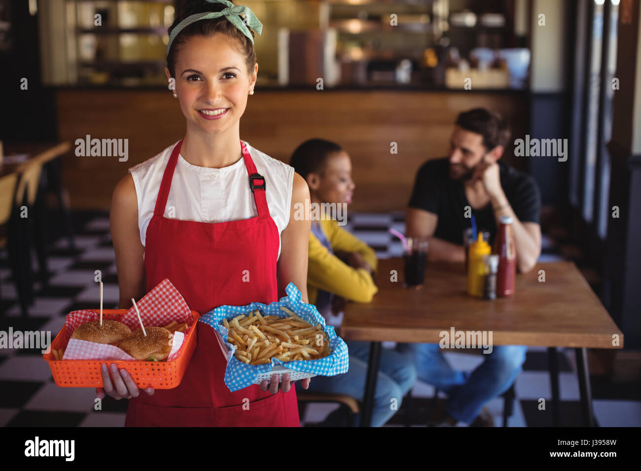 Portrait of a waitress holding burger and french fries in tray at ...