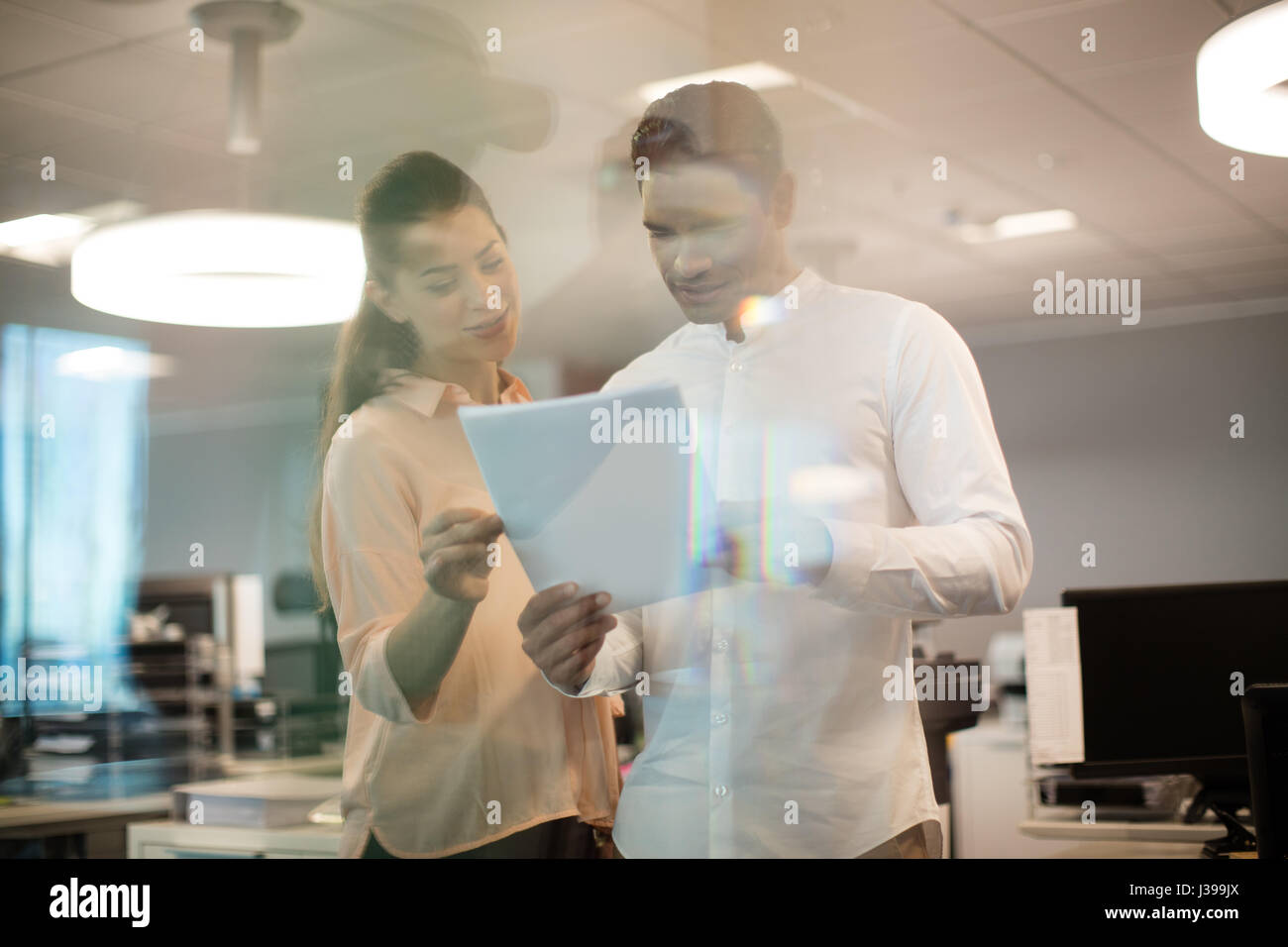 Business people discussing over documents seen through glass in office ...