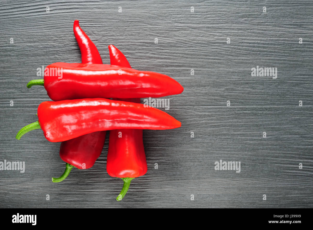 Five ripe sweet red Kapia peppers lying as sharp symbol on dark shale ...