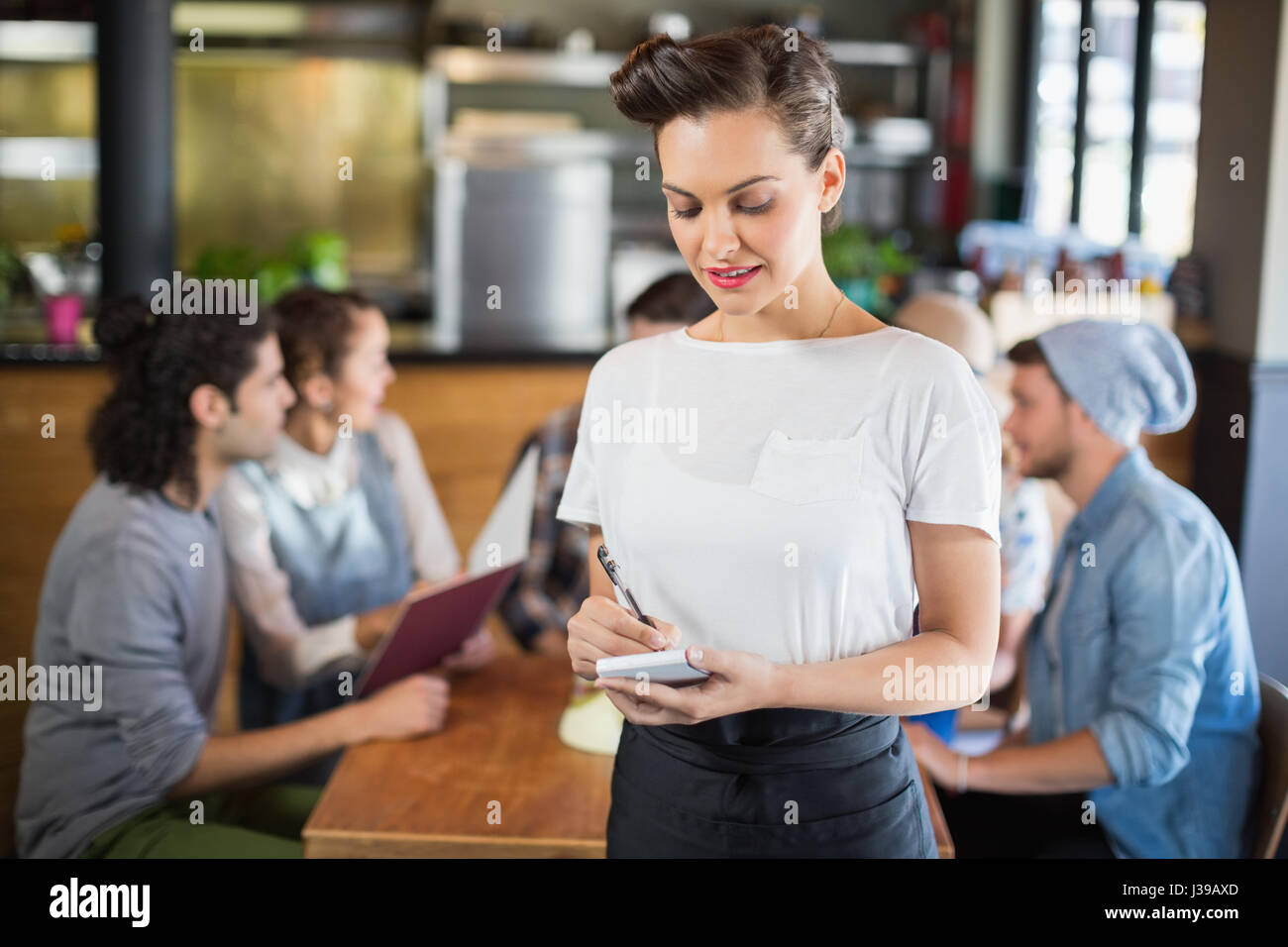 Beautiful waitress writing while standing by customers in restaurant ...
