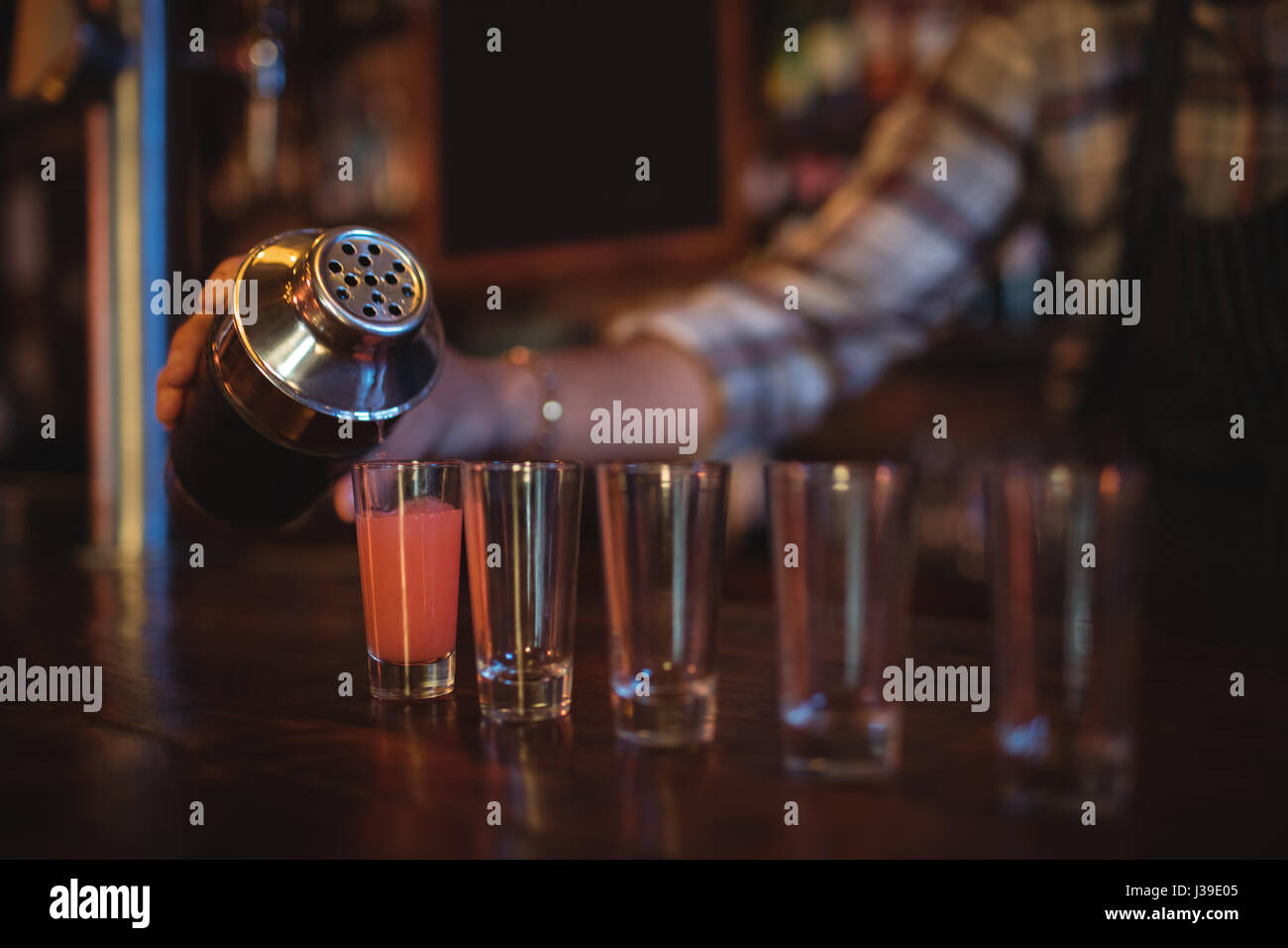 Waiter pouring cocktail drink into shot glasses at counter in bar Stock ...