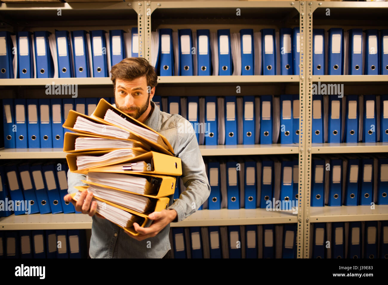 Businessman holding stack of files against cabinet in storage room ...