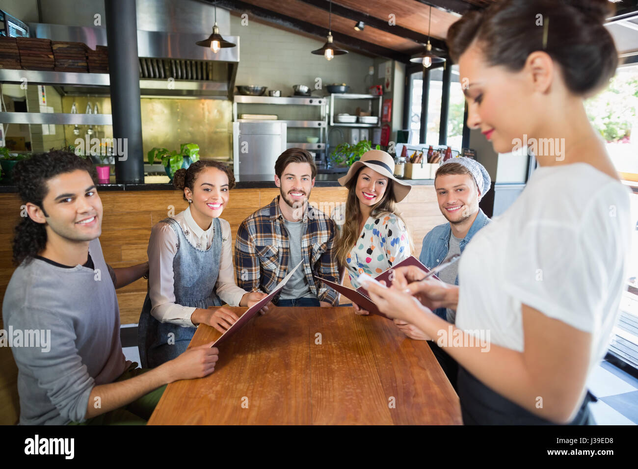 Portrait of friends sitting while waitress taking orders in restaurant ...