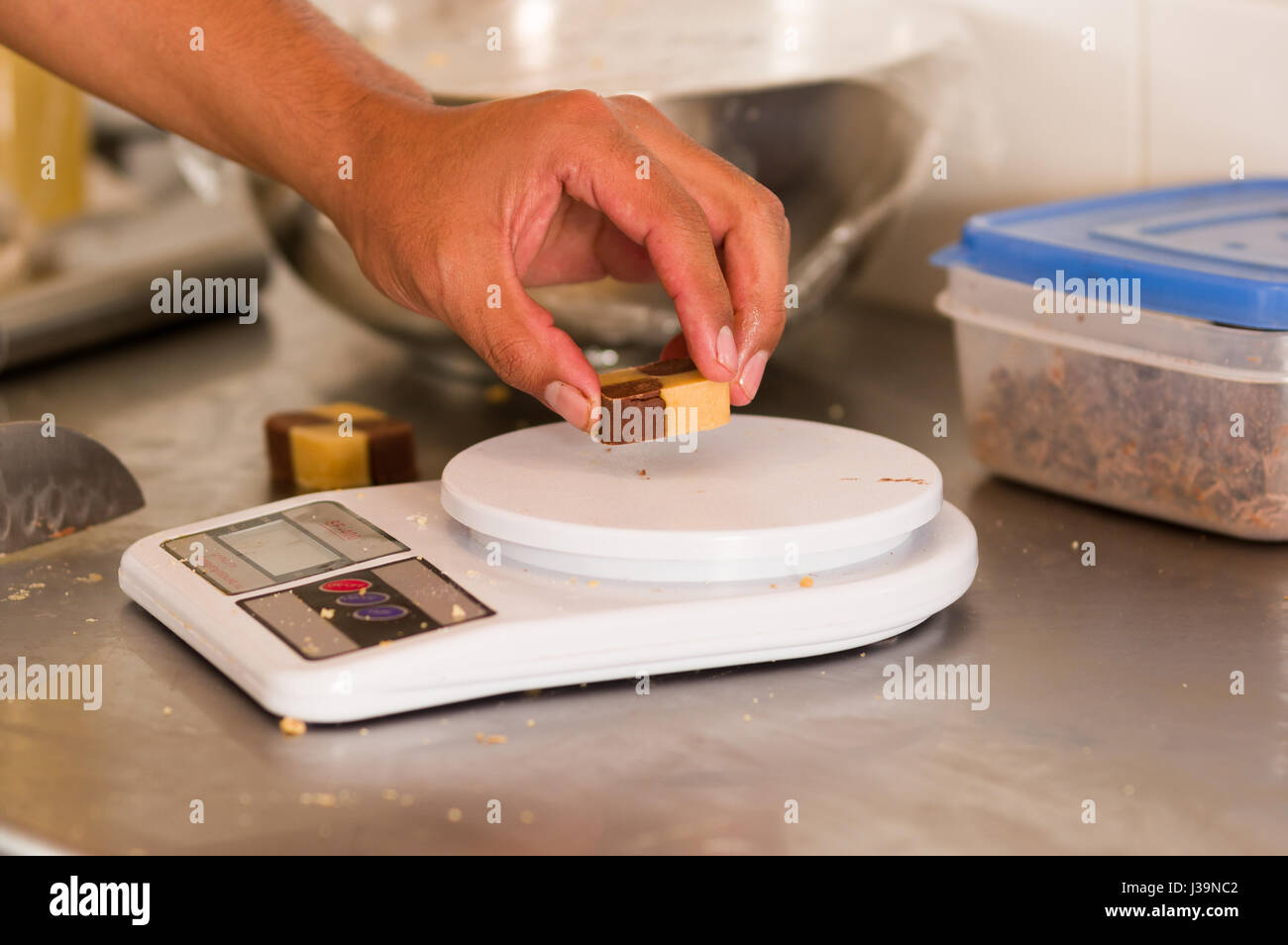 A man is using a food scale digital to weigh a cookie on metallic ...