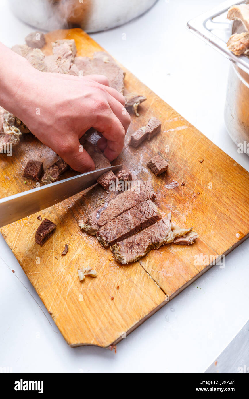 The cook cuts boiled beef meat on wooden cutting board Stock Photo - Alamy