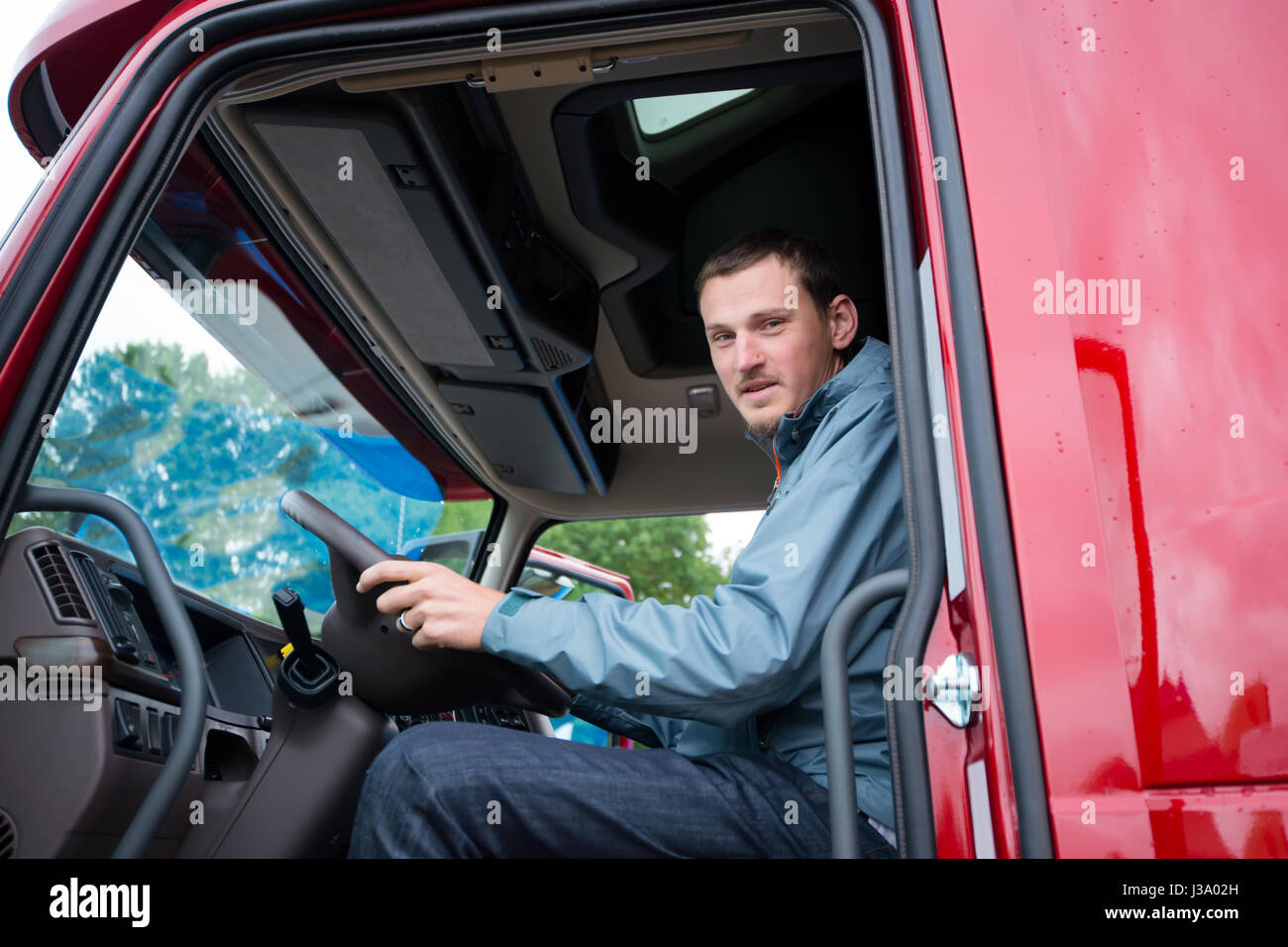 Happy truck driver sitting in the cab of red truck behind the wheel and ...