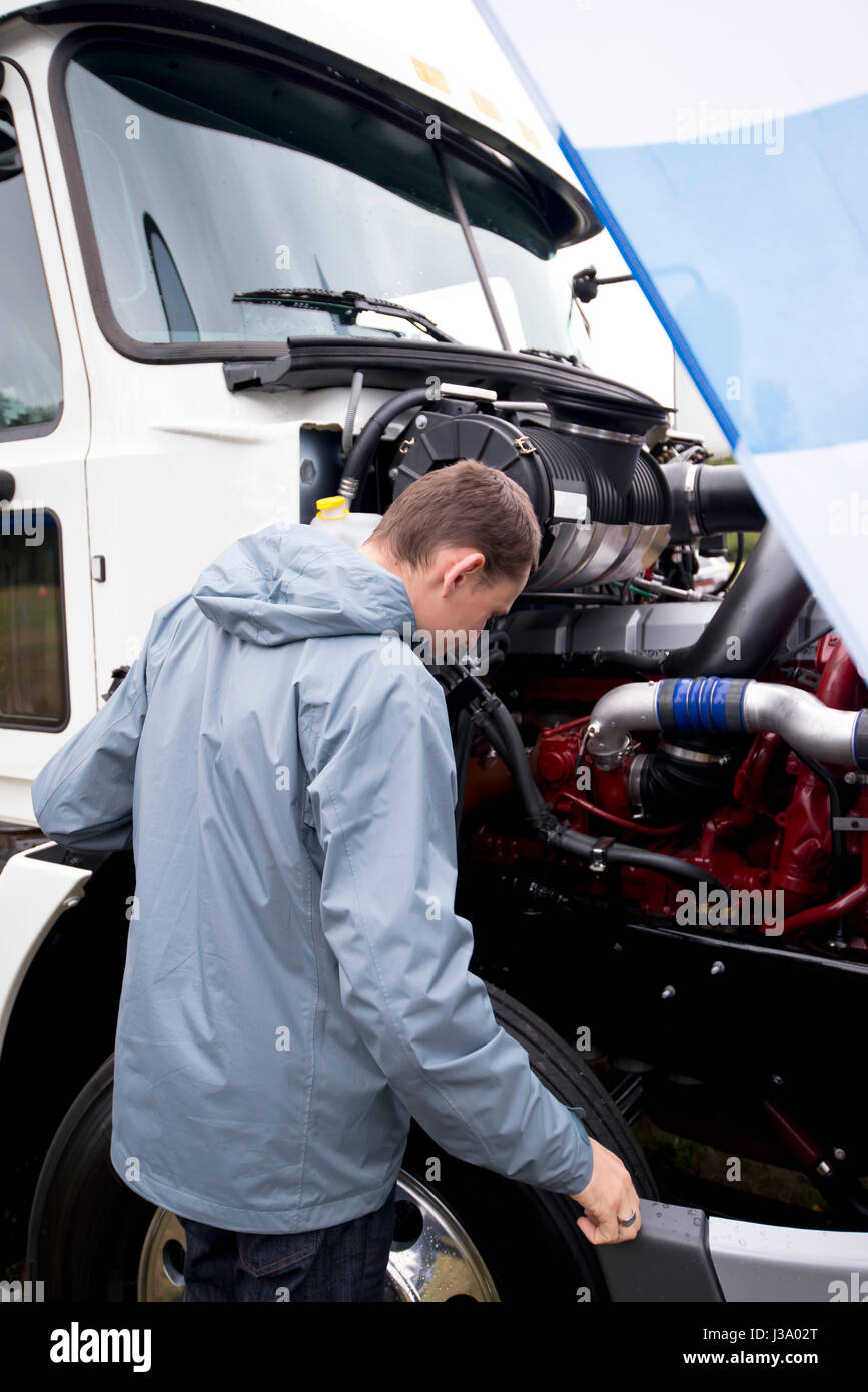 Truck driver in a gray jacket with hood checking the operation status ...