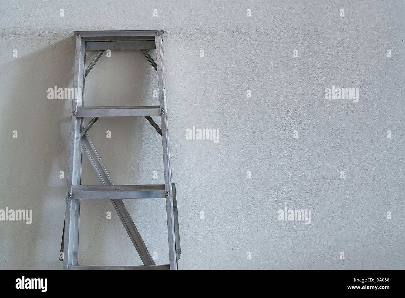 Aluminum ladder on the gray wall, room interior Stock Photo - Alamy