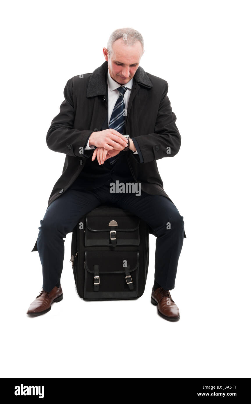 Middle age business man checking time sitting on carry on luggage ...