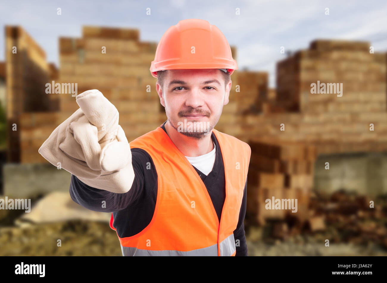Smiling young builder pointing finger at you outdoors on construction ...