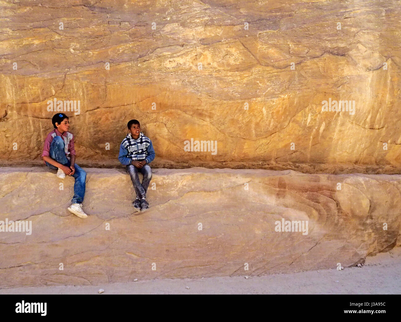 Two local boys sitting on aquaduct (water channels) along cliff of the ...