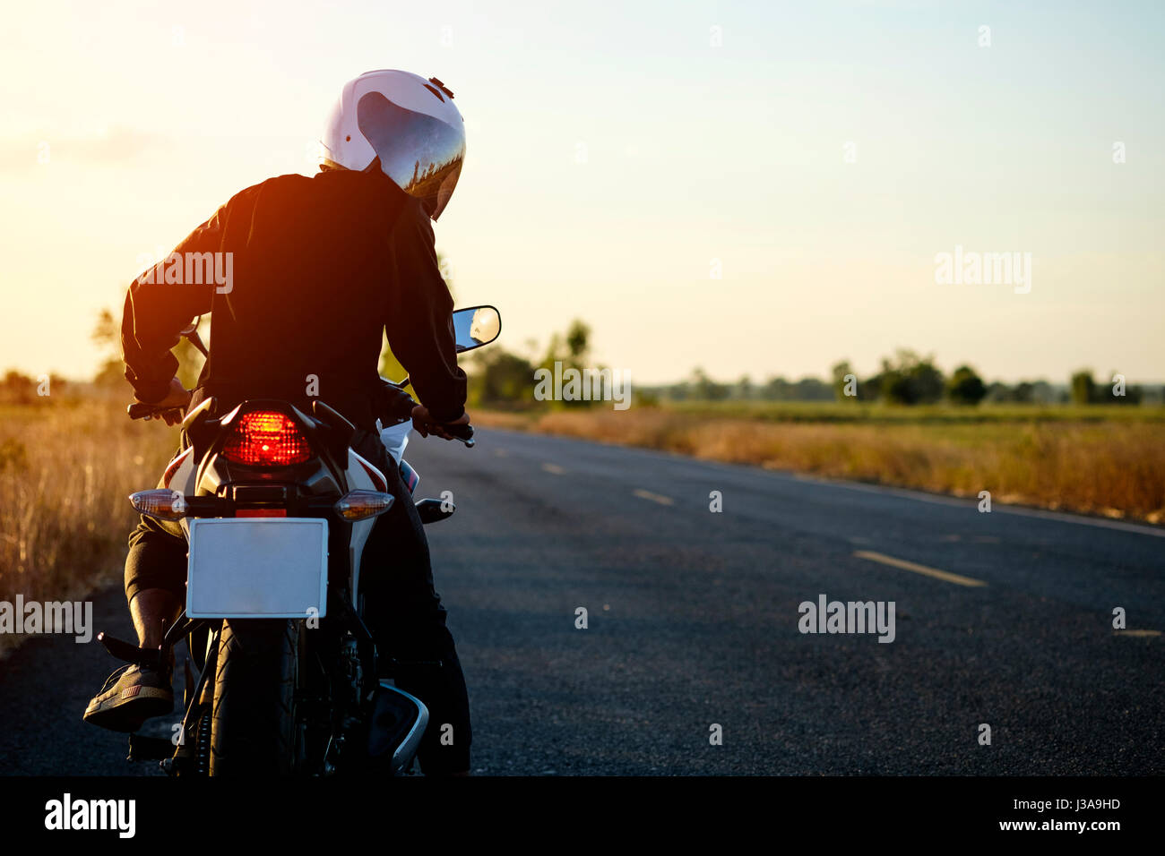 a man on the motorcycle parking on the road left side and sunset, to ...