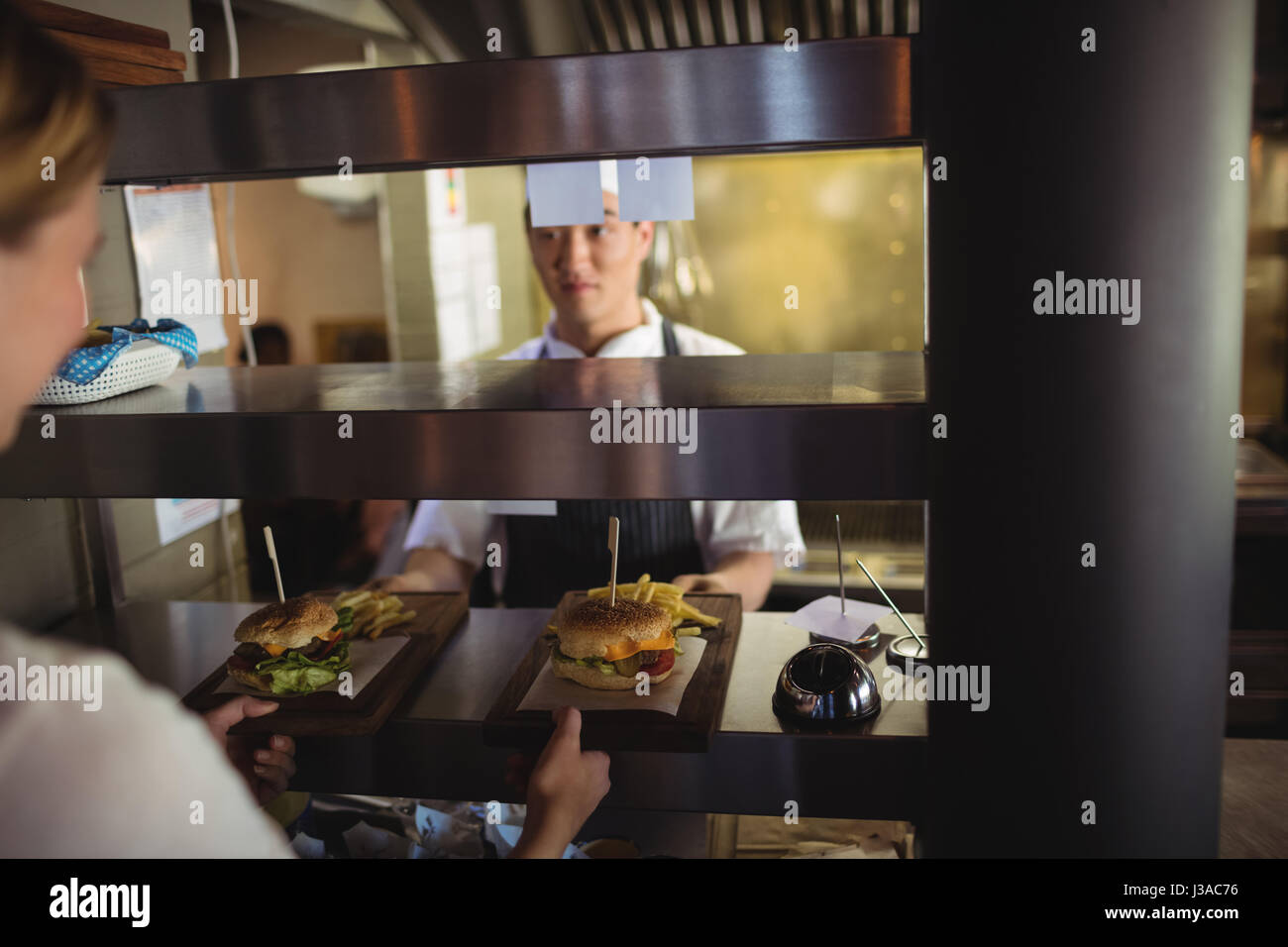 Chef passing tray with french fries and burger to waitress in the ...