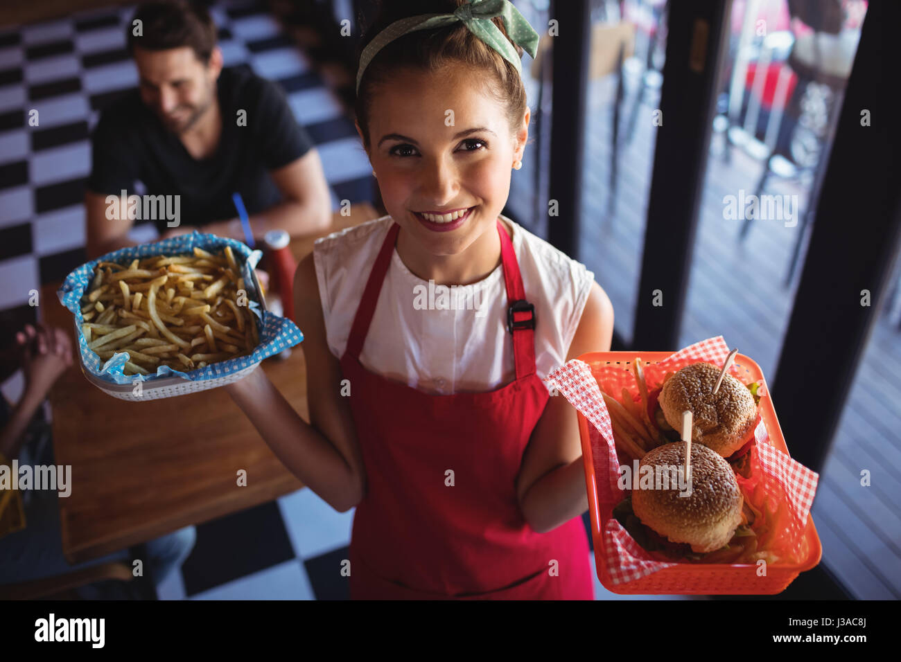 Portrait of a waitress holding burger and french fries in tray at ...