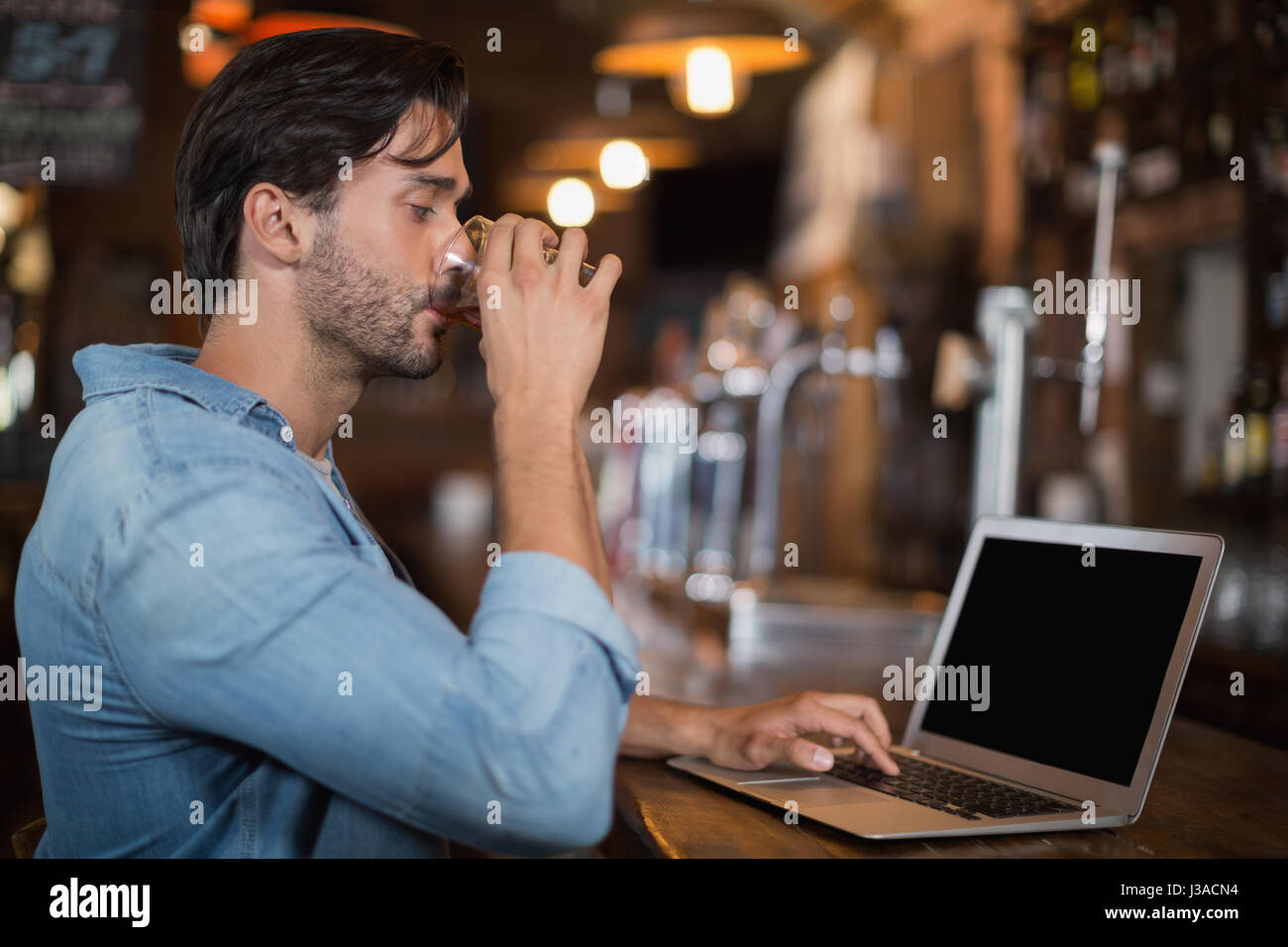 Young man drinking beer while using laptop in restarant Stock Photo - Alamy