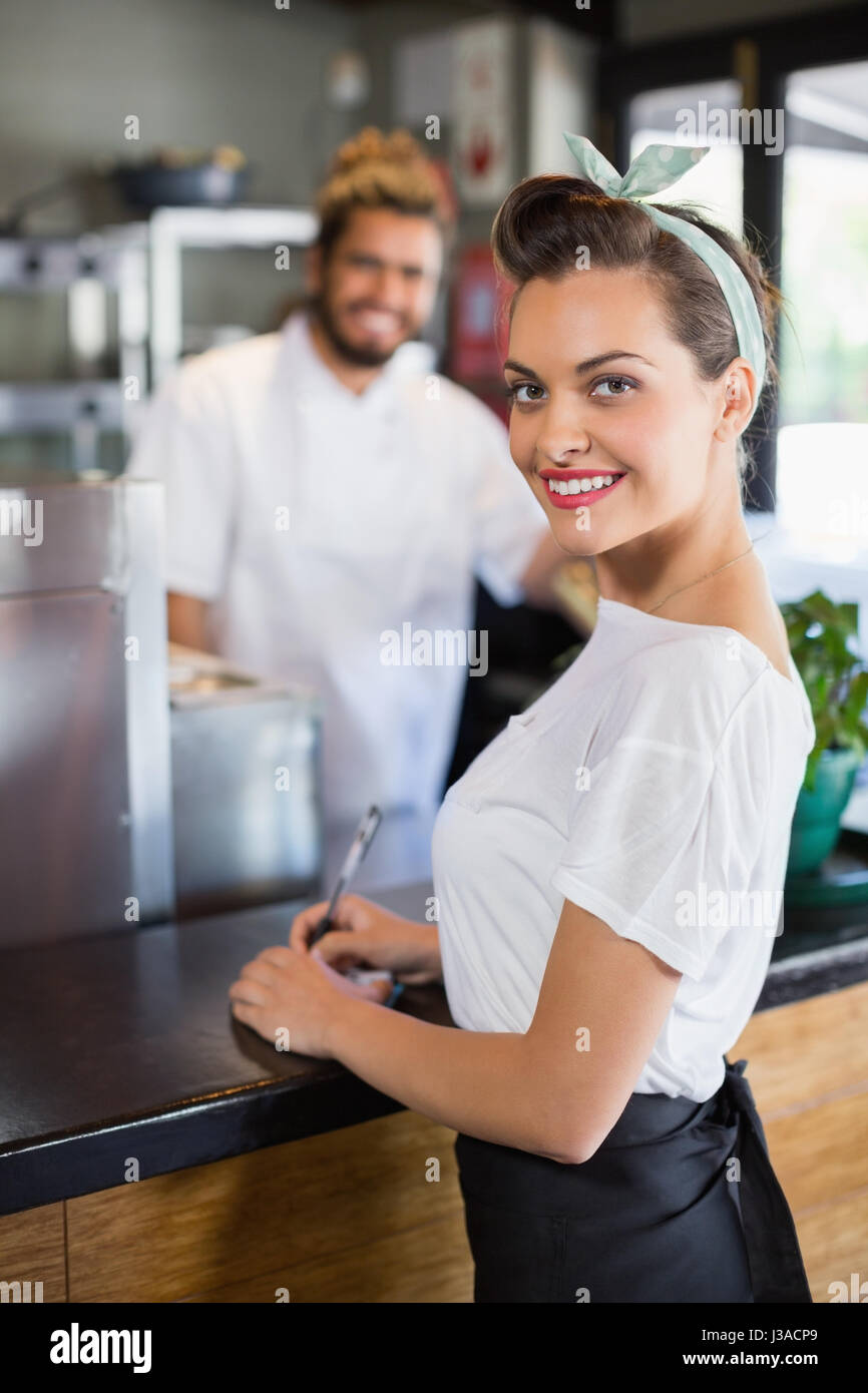 Smiling waitress writing on notepad with chef in background Stock Photo ...