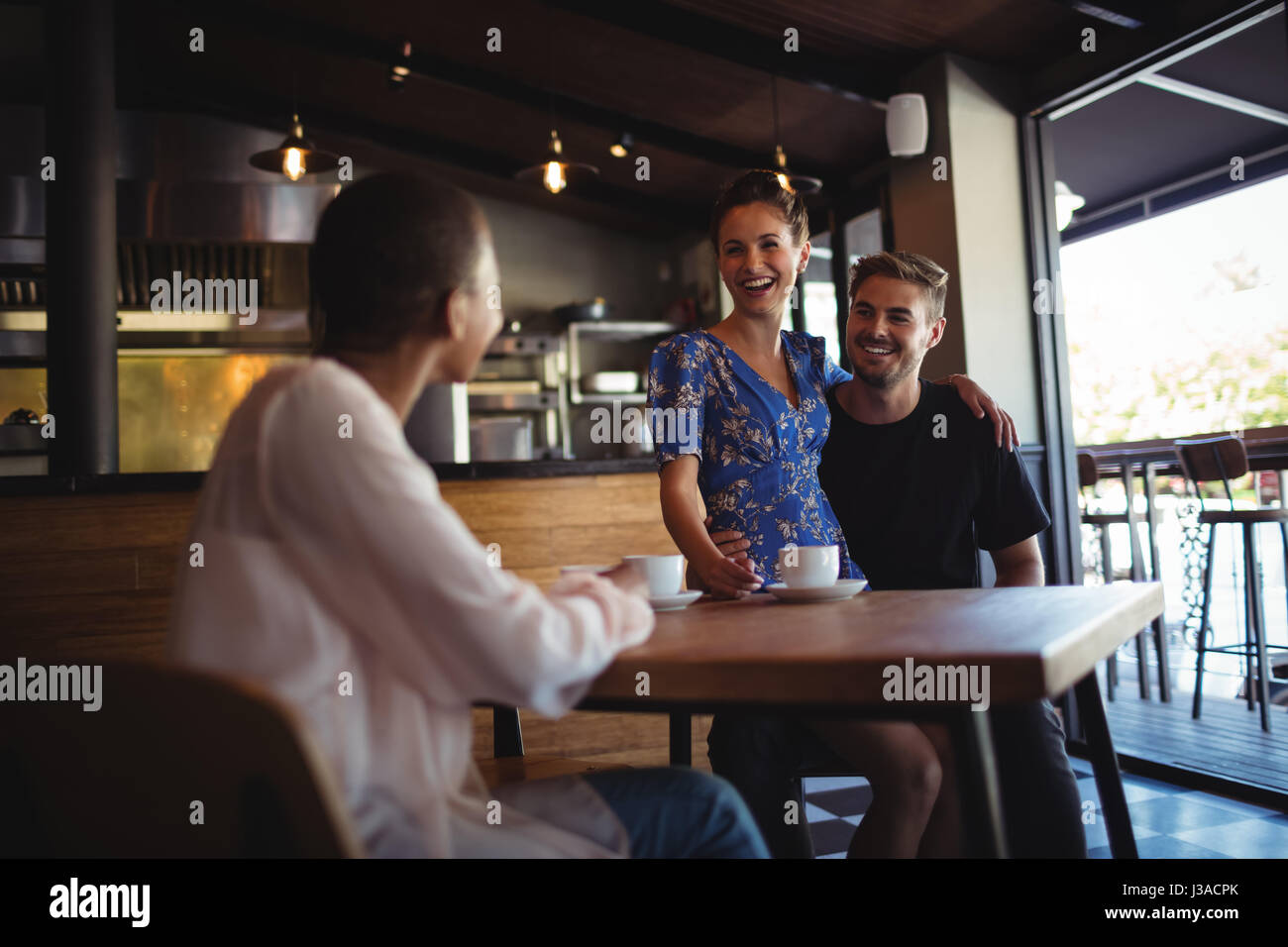 Friend interacting with happy couple while having coffee in restaurant Stock Photo - Alamy
