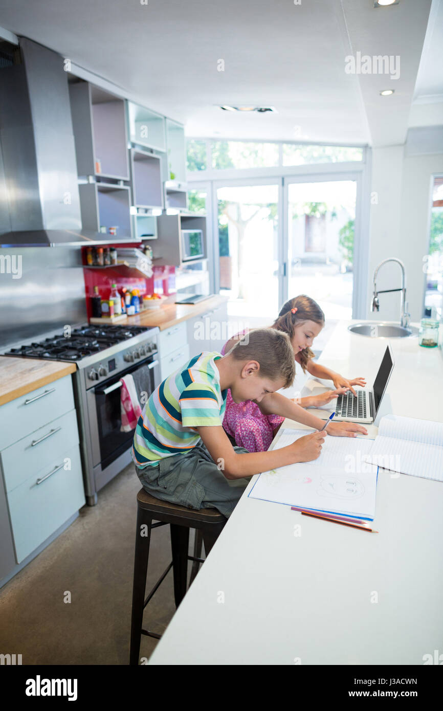 Boy doing his homework while girl using laptop in kitchen at home Stock ...
