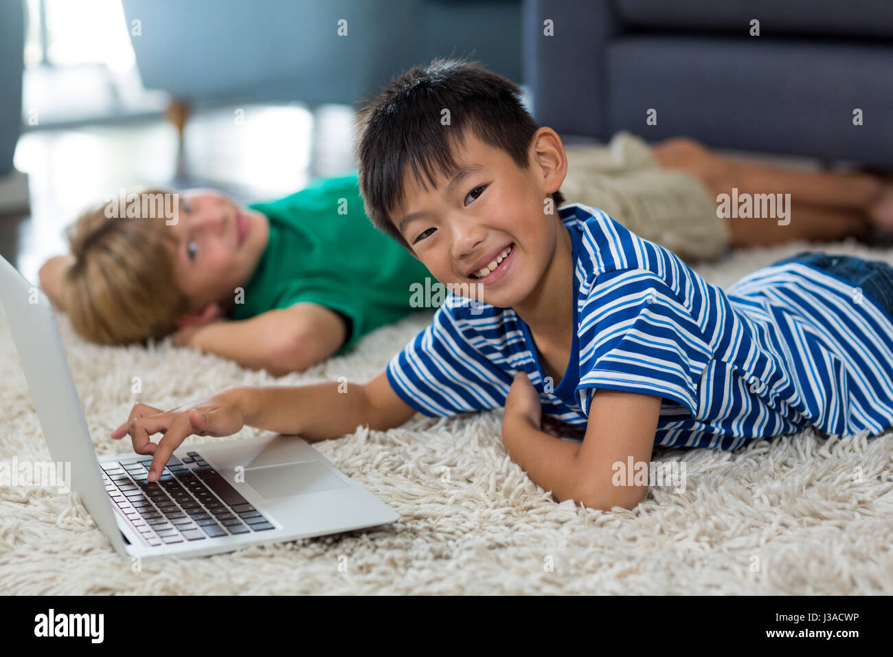 Boy lying on rug and using laptop in living room at home Stock Photo ...