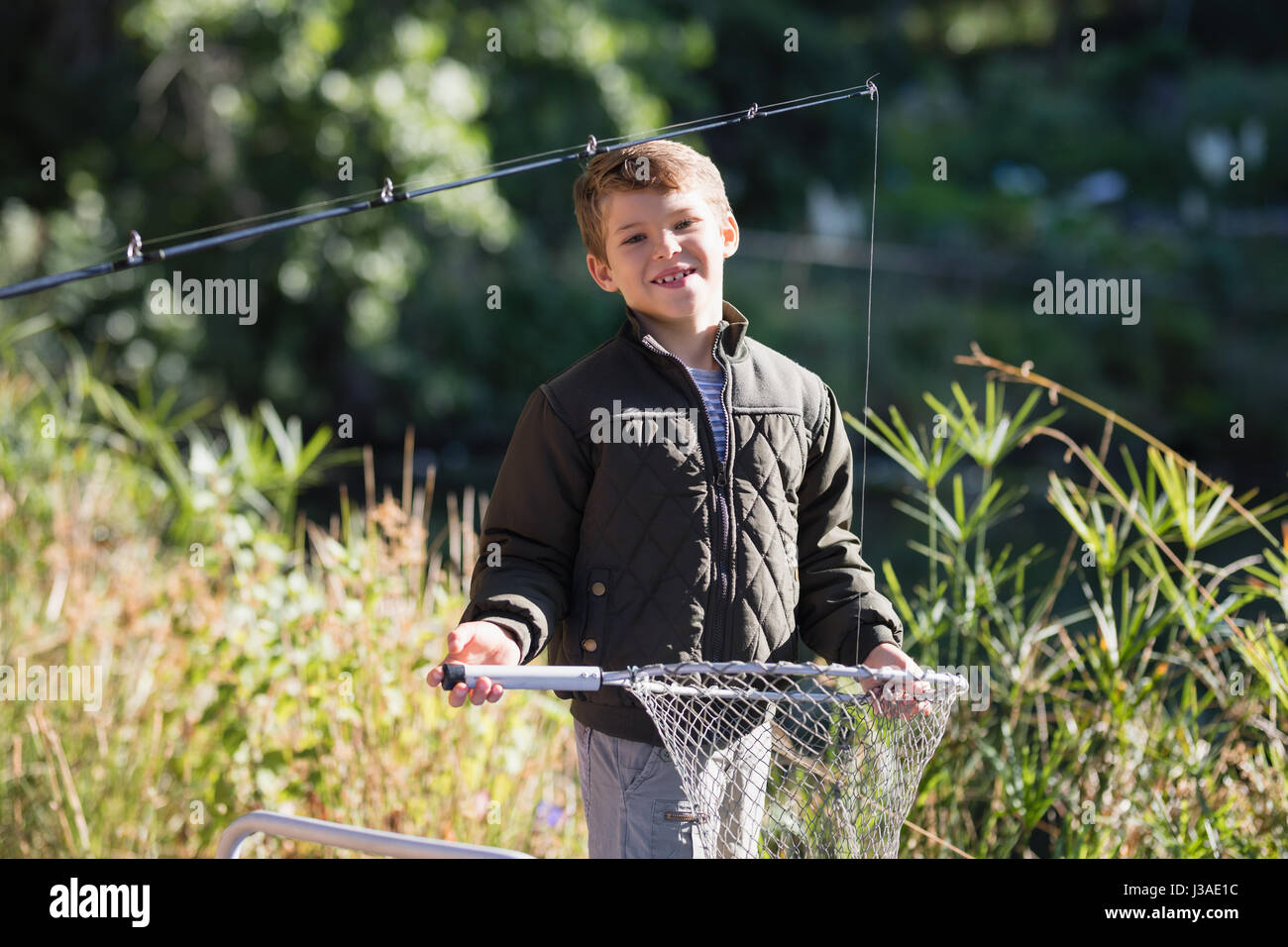 Portrait of smiling boy holding fishing net while standing in forest on ...